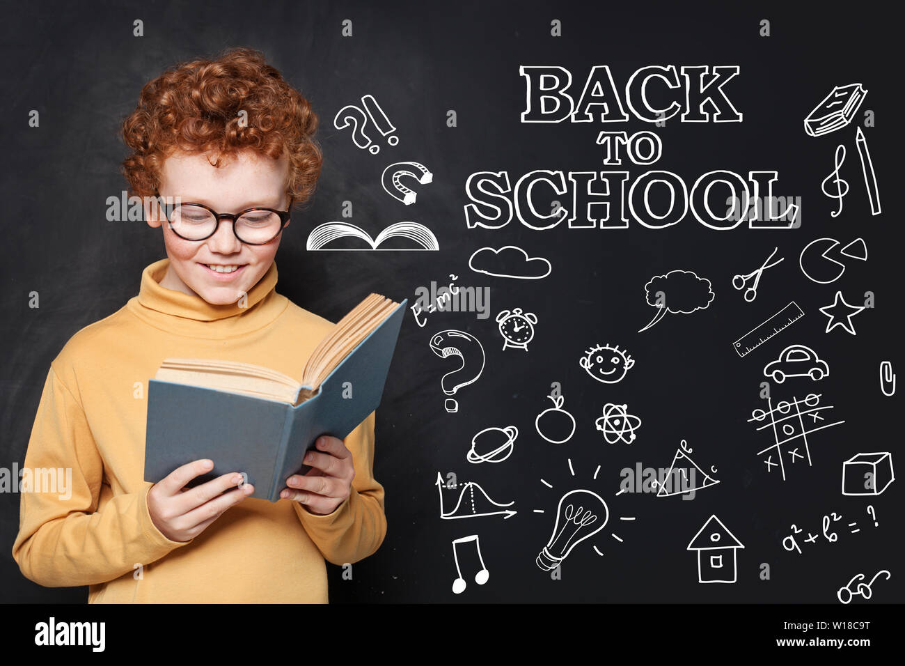 Happy child reading a book in classroom on chalkboard background. Back ...