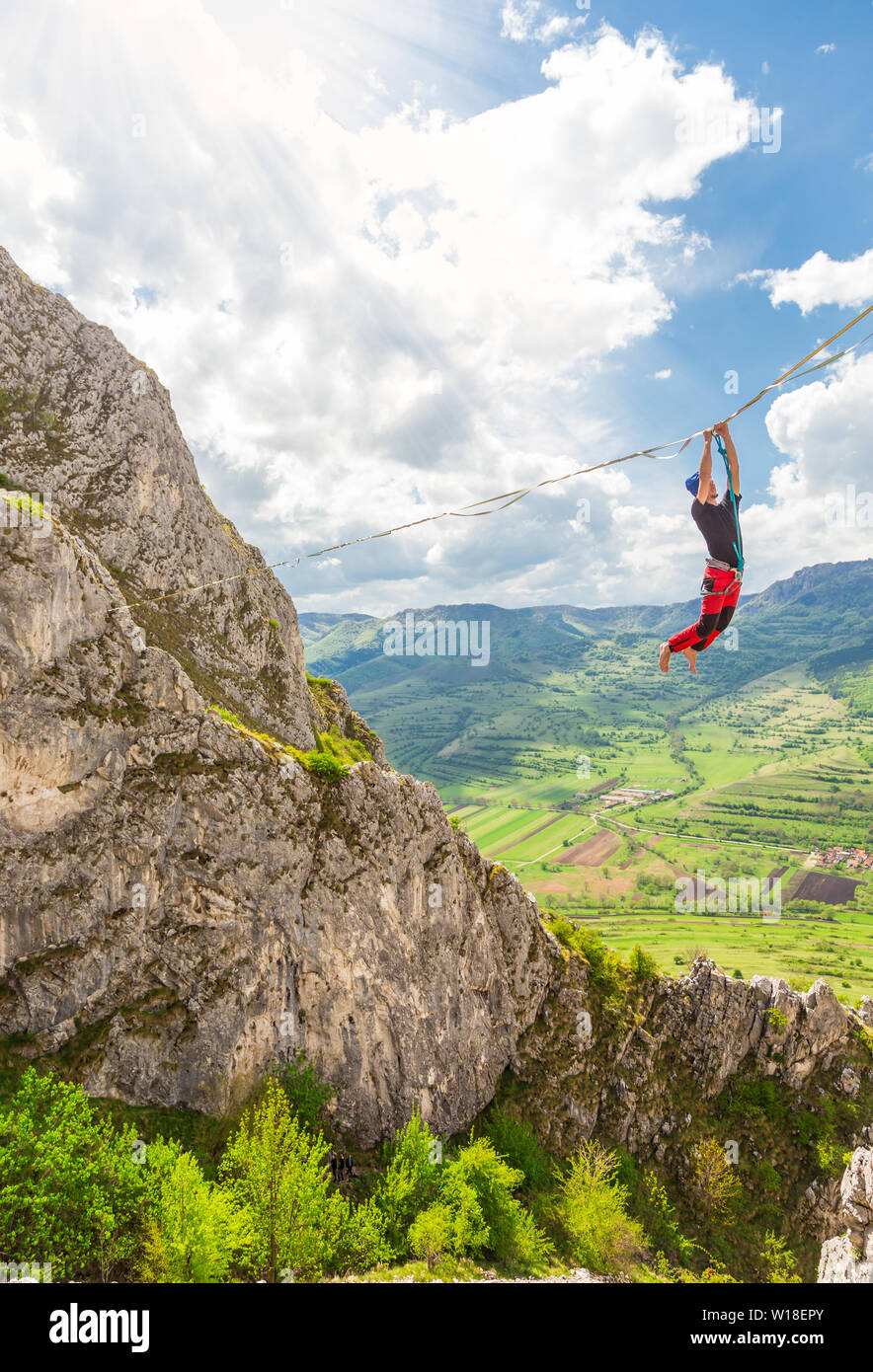 Young slackliner man hanging on a slackline betweend two rocks ...