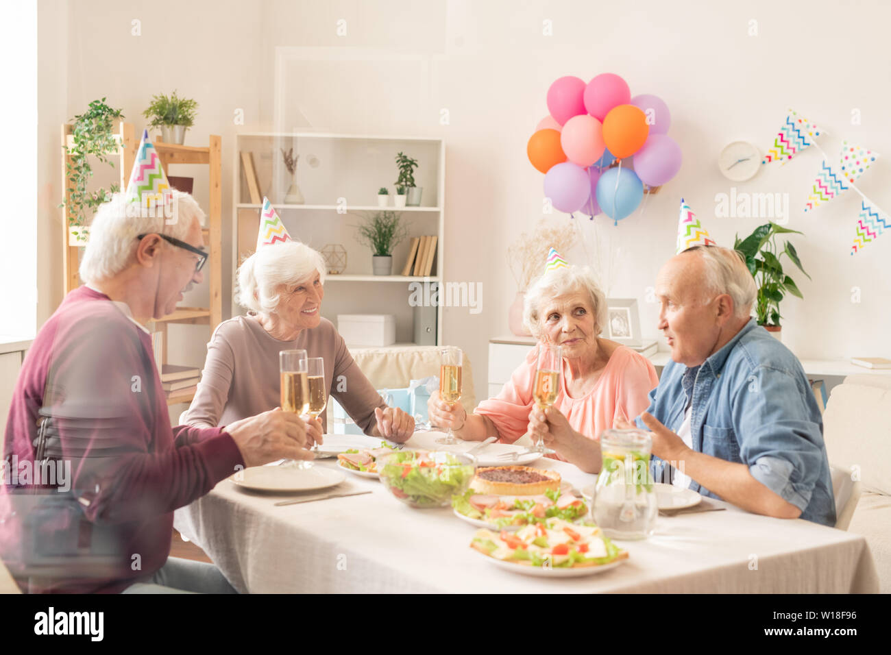 Four senior friends with champagne sitting by festive table during home ...