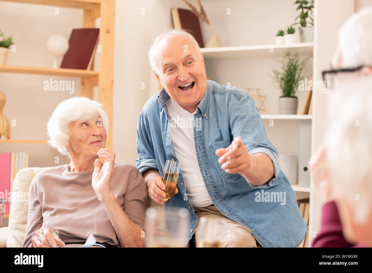 Happy senior man with flute of champagne pointing at his friend during ...