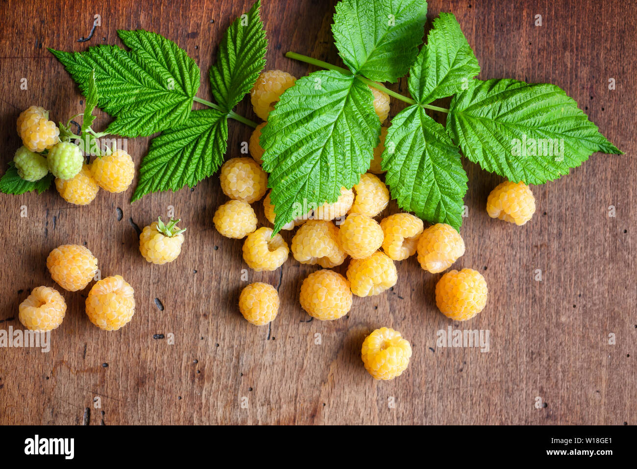 Ripe yellow raspberries with leaves on the old wooden background. Top ...