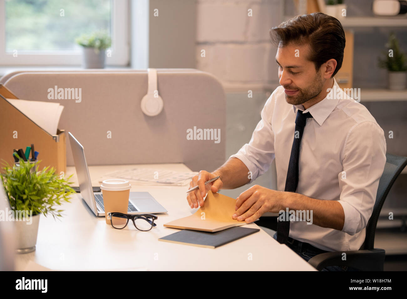 Content handsome young white-collar man sitting at desk in modern ...