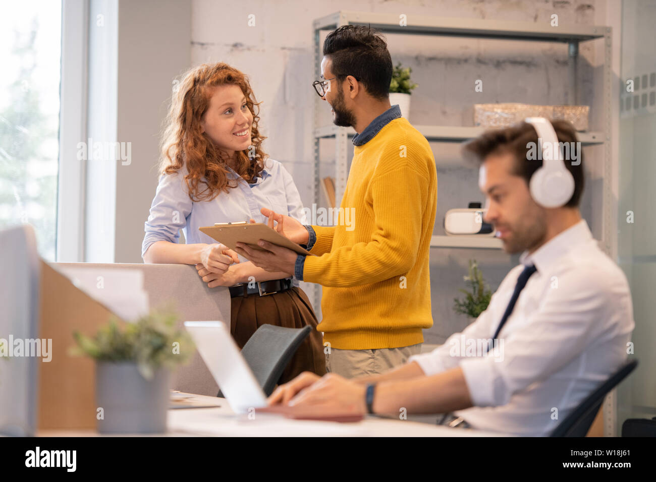 Positive creative young multi-ethnic colleagues standing in open-space ...