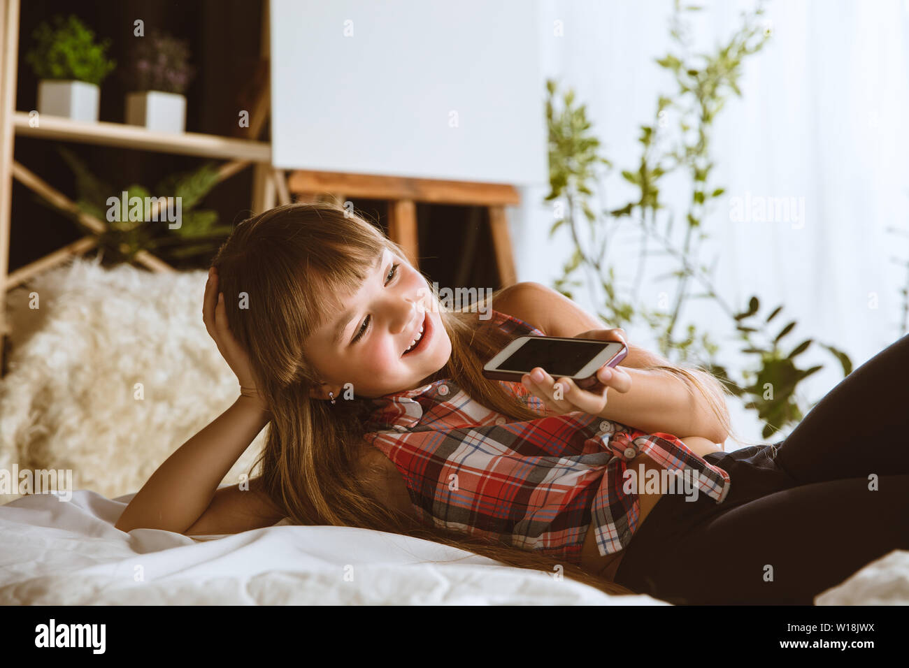 Girl using different gadgets at home. Little model lying in her bed ...