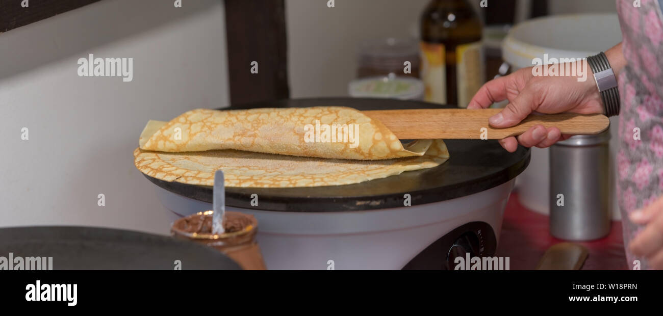 Prepare crepes on a hot plate and fold with a long wooden spoon Stock ...