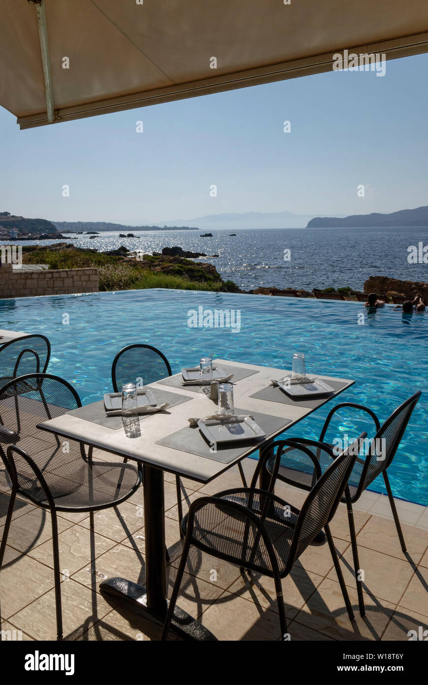 Crete, Greece. June 2019. Poolside restaurant table and chairs overlook ...