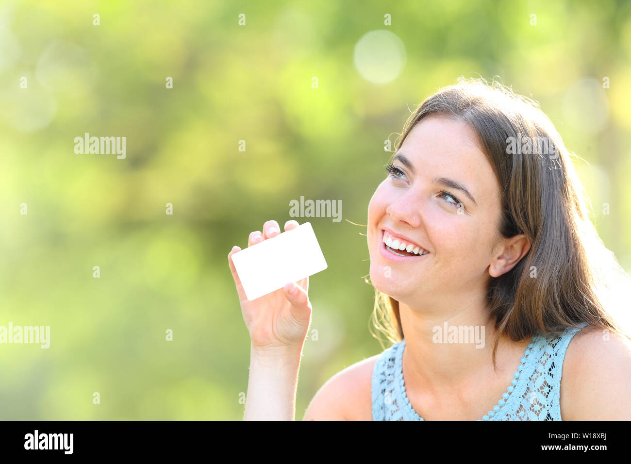 Happy woman showing blank credit card looking at side in a park with a ...