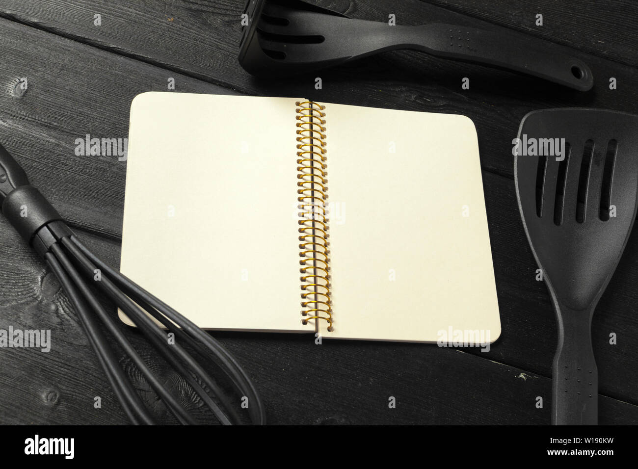 Blank sheet of opened notepad and kitchen utensils on table with ...