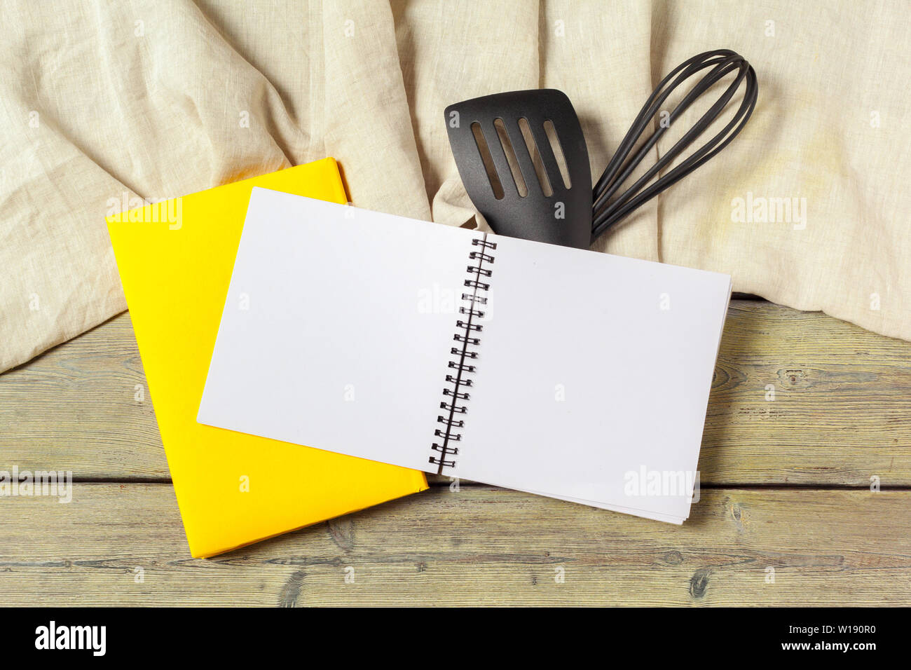 Blank sheet of opened notepad and kitchen utensils on table with ...