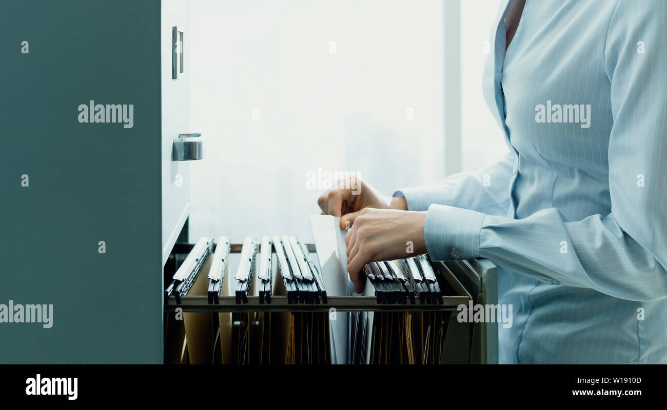 Professional female office clerk searching files and paperwork in the ...