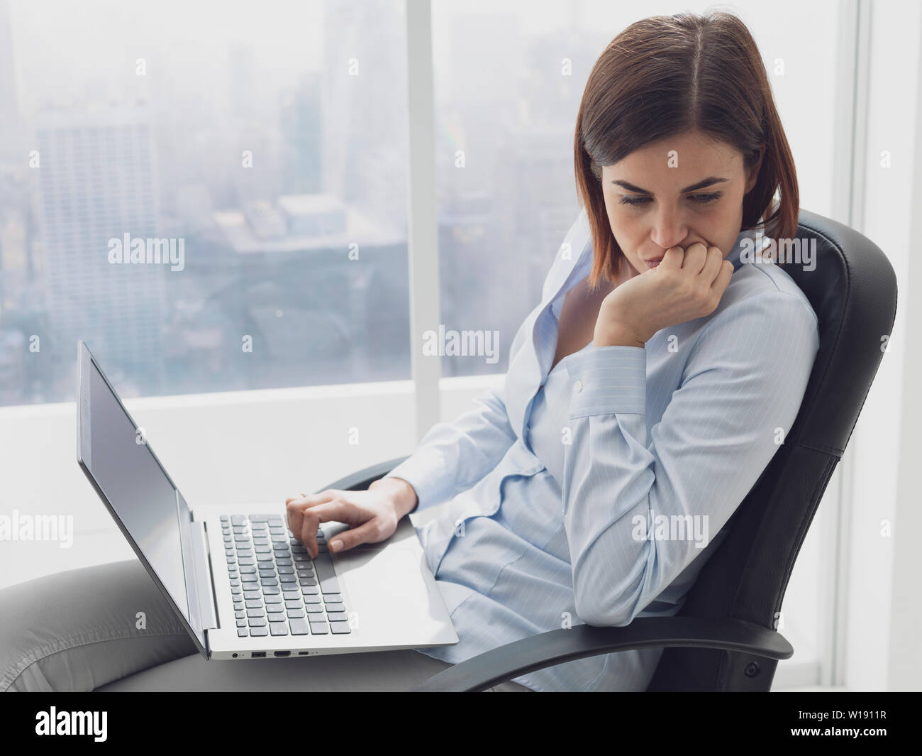 Pensive businesswoman working in the office with a laptop on her lap ...