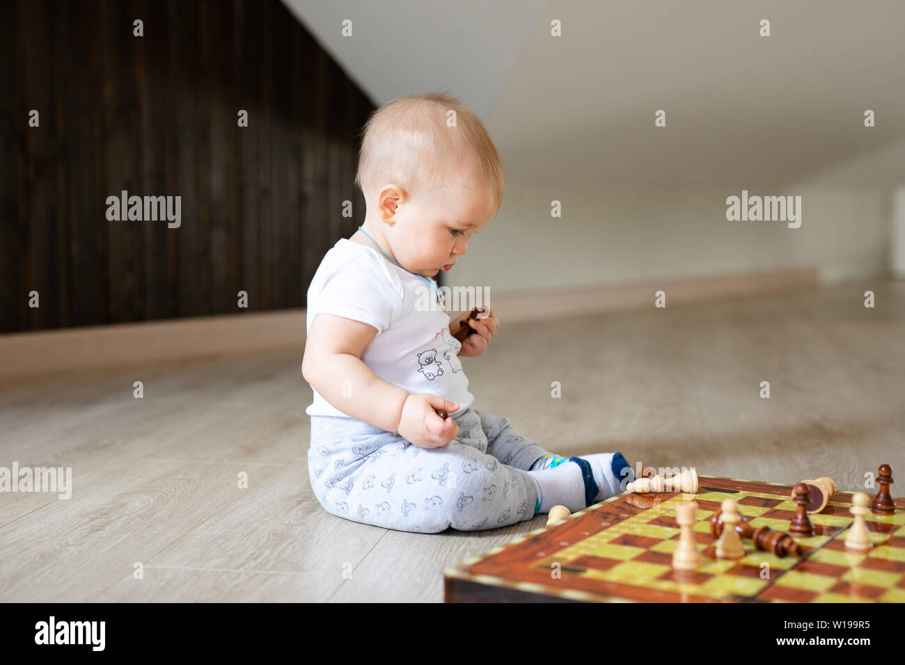 Two babies boy and girl playing chess on the white wooden floor at home ...