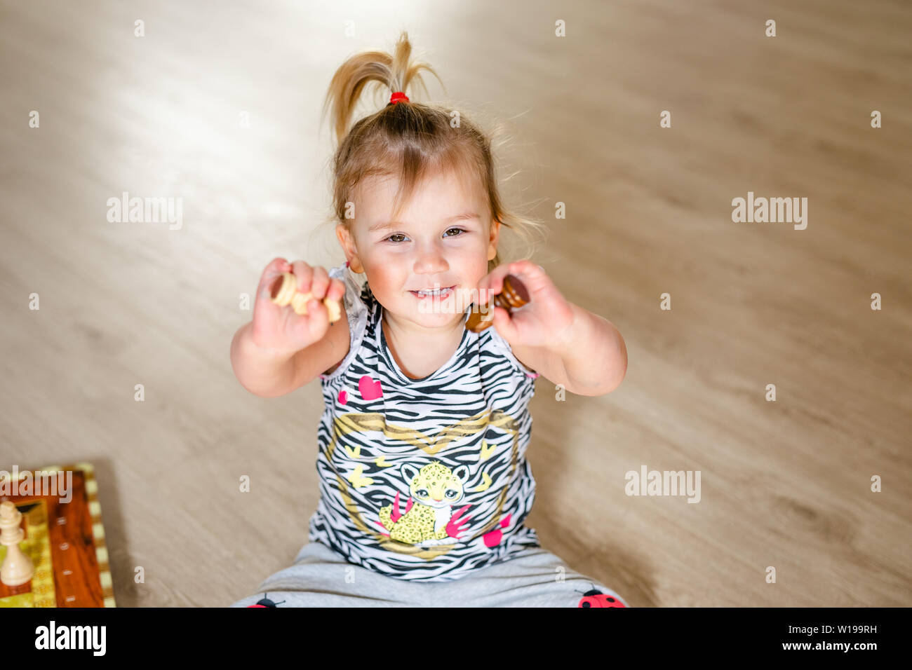 Two babies boy and girl playing chess on the white wooden floor at home ...