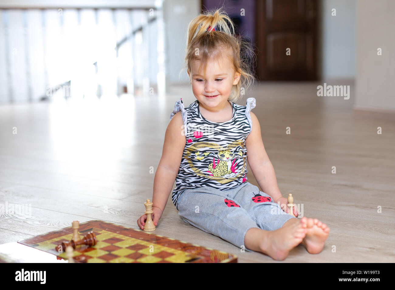 Two babies boy and girl playing chess on the white wooden floor at home ...