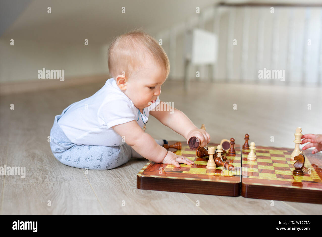 Two babies boy and girl playing chess on the white wooden floor at home ...