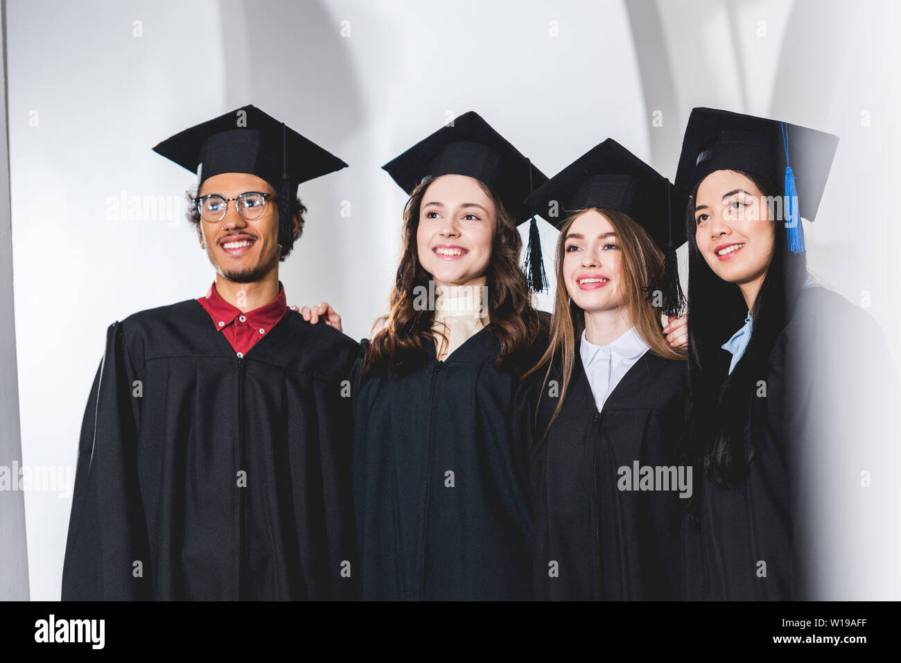 group of cheerful students in graduation caps smiling in university ...