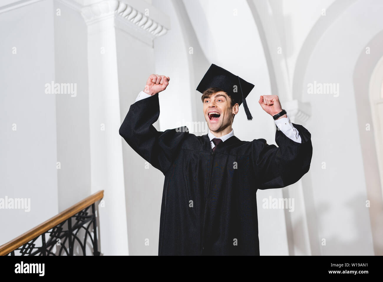 happy young man in graduation cap smiling and gesturing in university ...