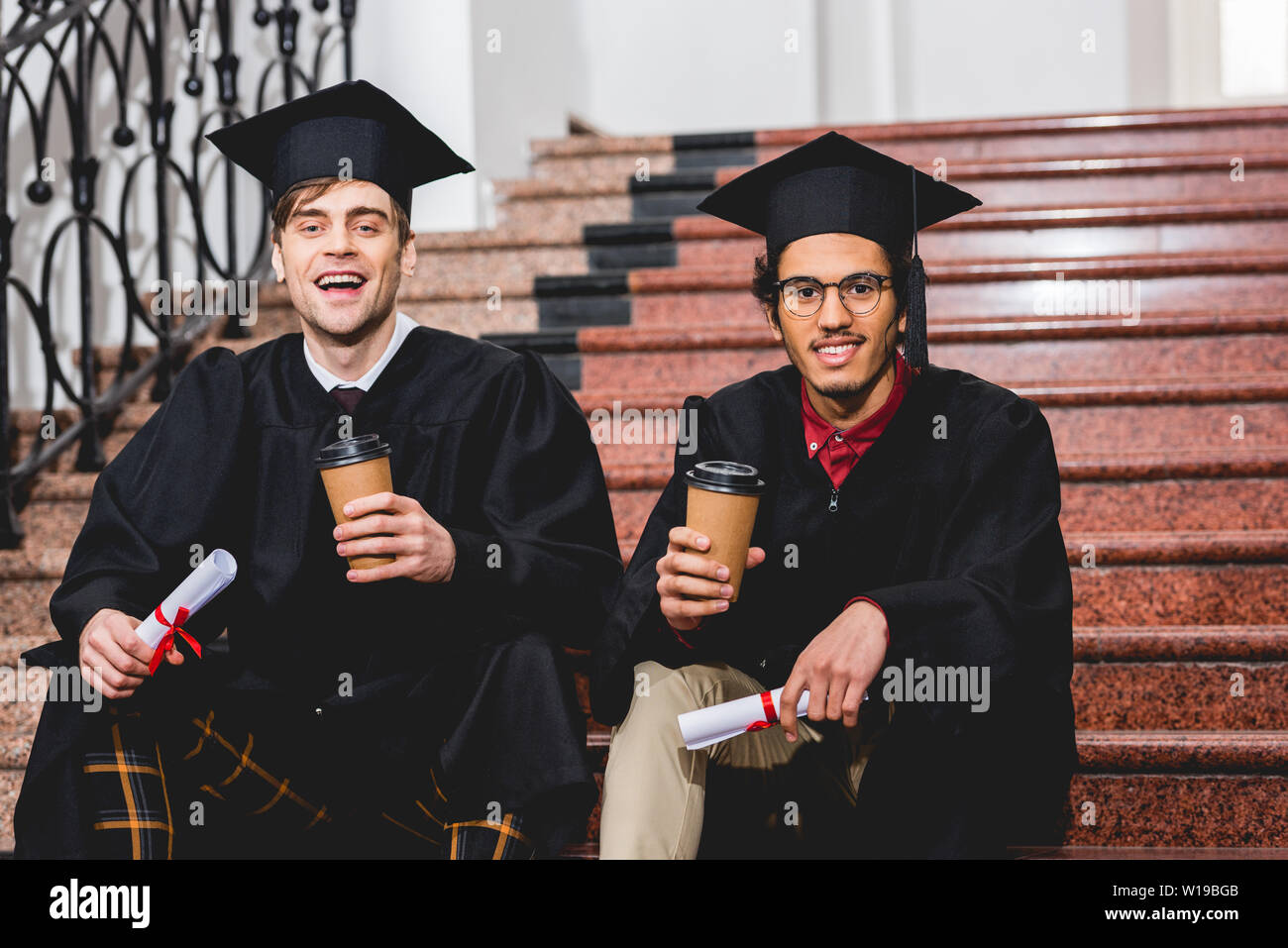 cheerful students in graduation caps holding diplomas and paper cups ...