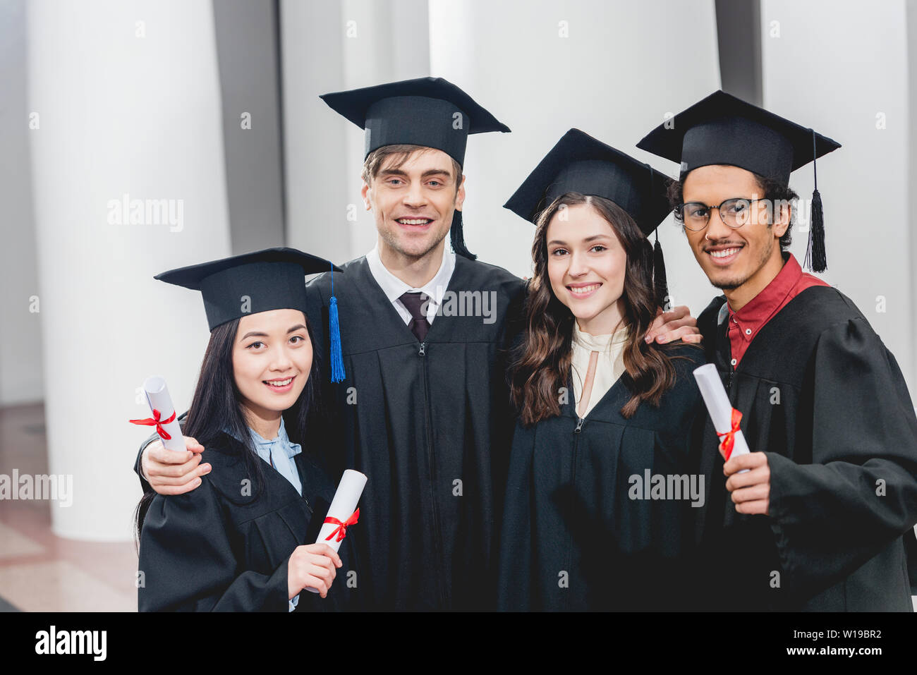 smiling group on students looking at camera while holding diplomas ...