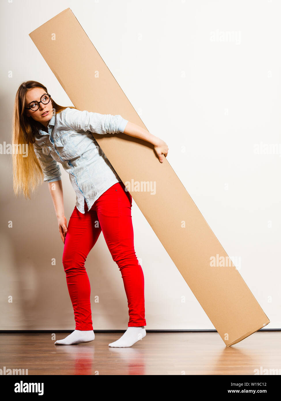 Woman moving into new apartment house carrying heavy carton box with ...