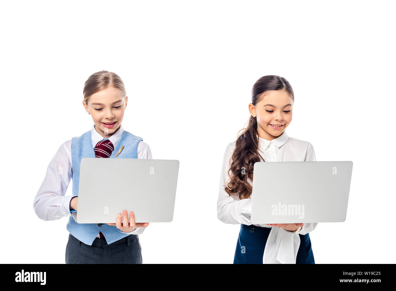 smiling schoolgirls in formal wear using laptops Isolated On White ...