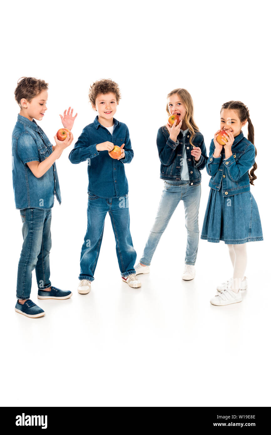 full length view of children in denim clothes eating apples on white ...