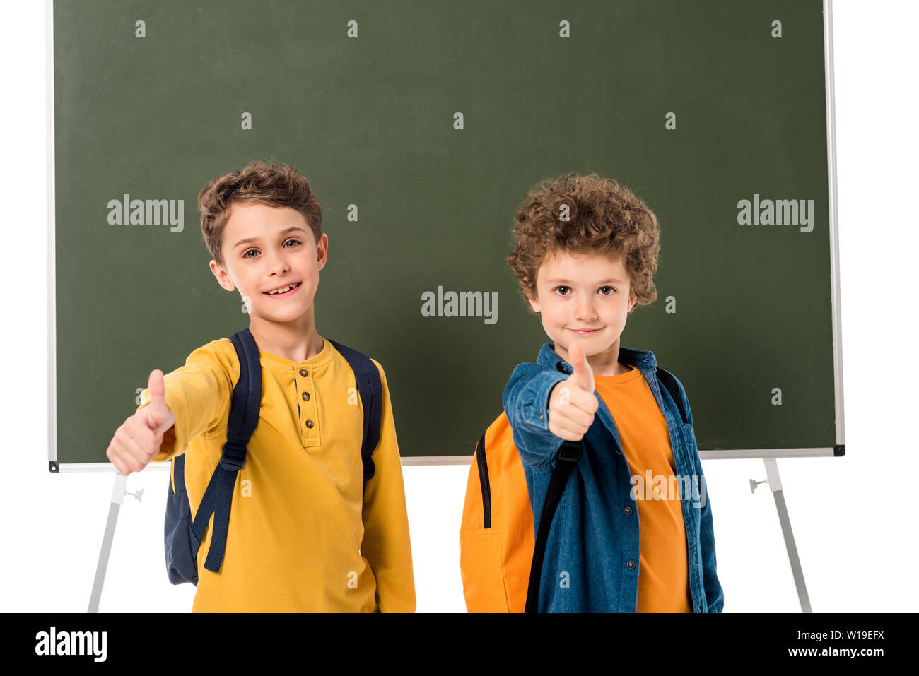 front view of two schoolboys with backpacks standing near blackboard ...