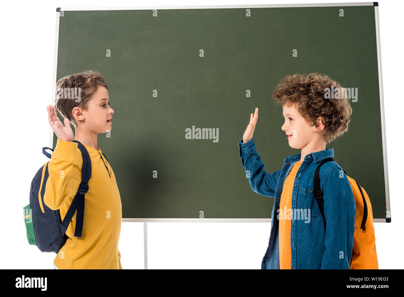 two smiling schoolboys with backpacks showing high five sign near ...