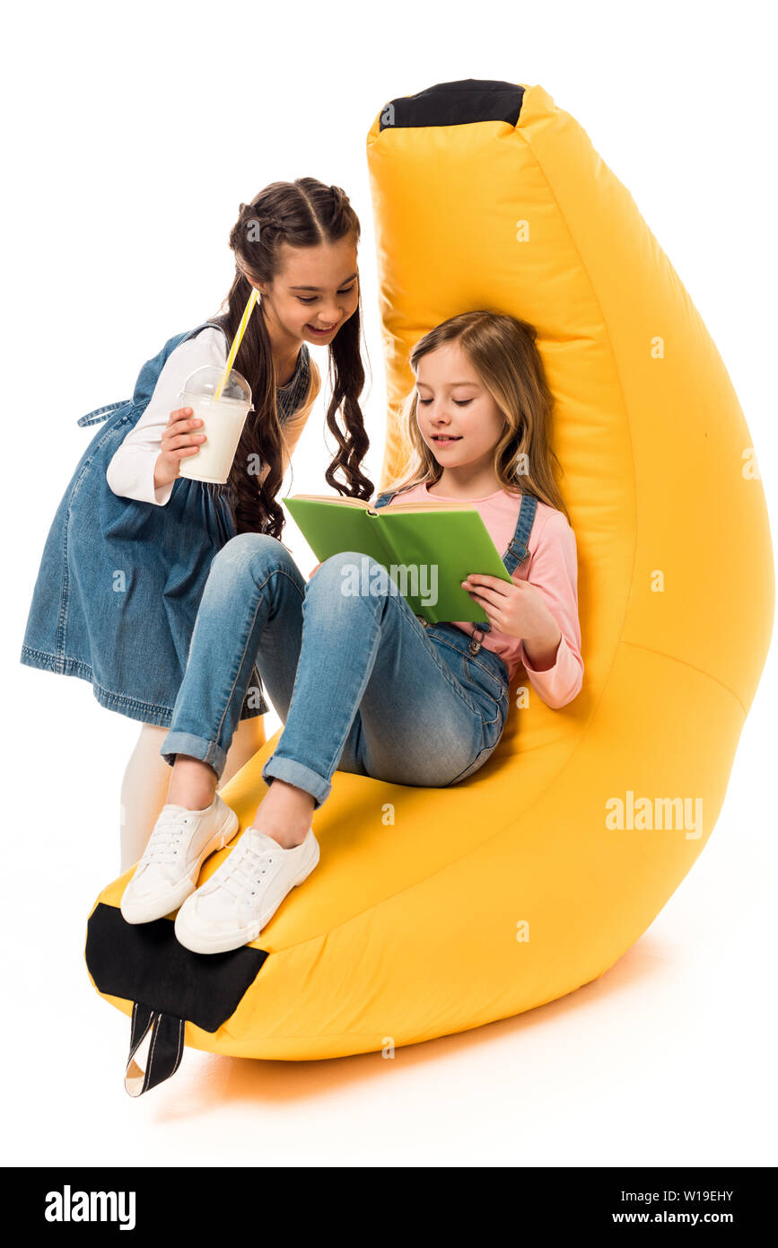 two smiling kids with bean bag chair reading book on white Stock Photo ...