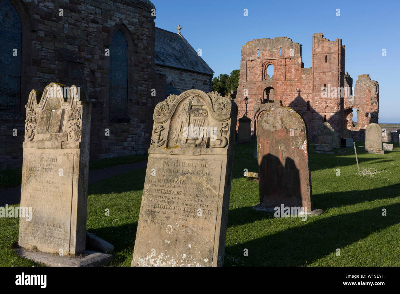 Church gravestones and the ruined monastery walls of Lindisfarne priory ...