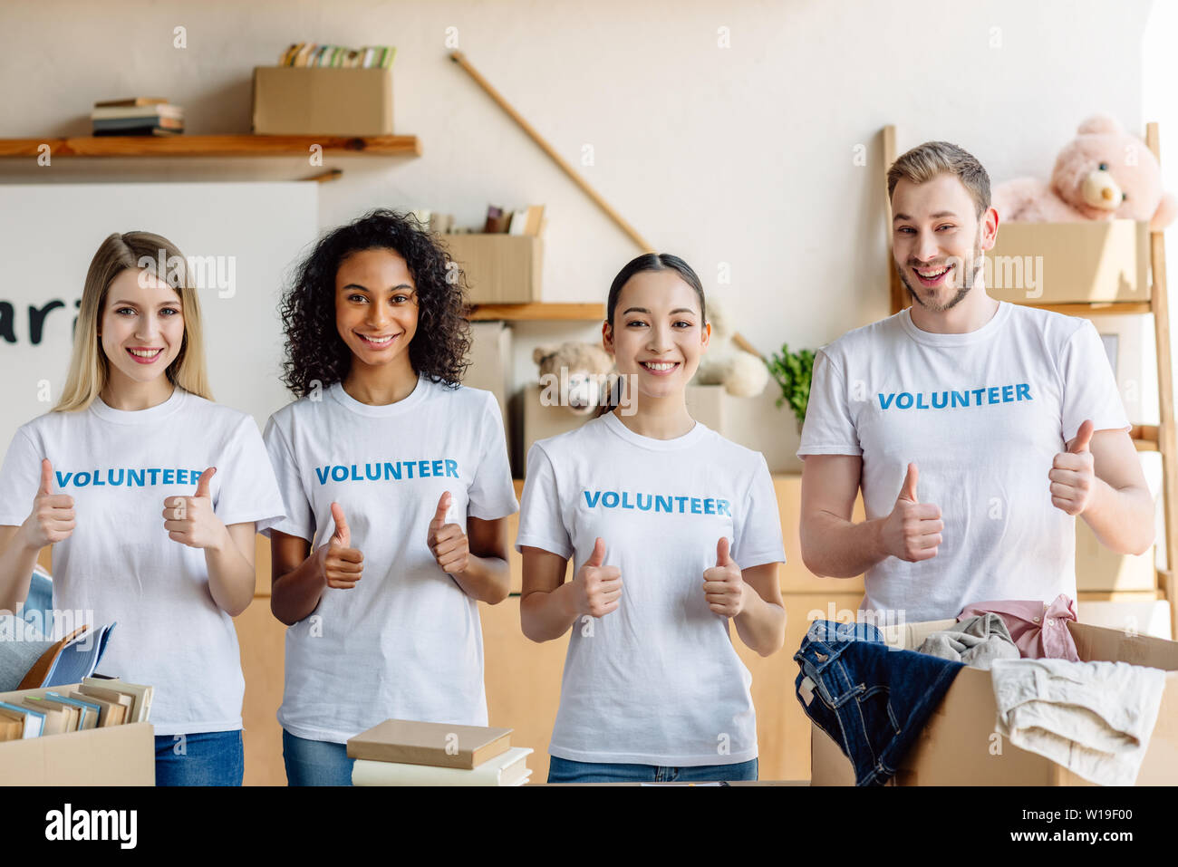 group of four smiling young volunteers in white t-shirts with volunteer ...