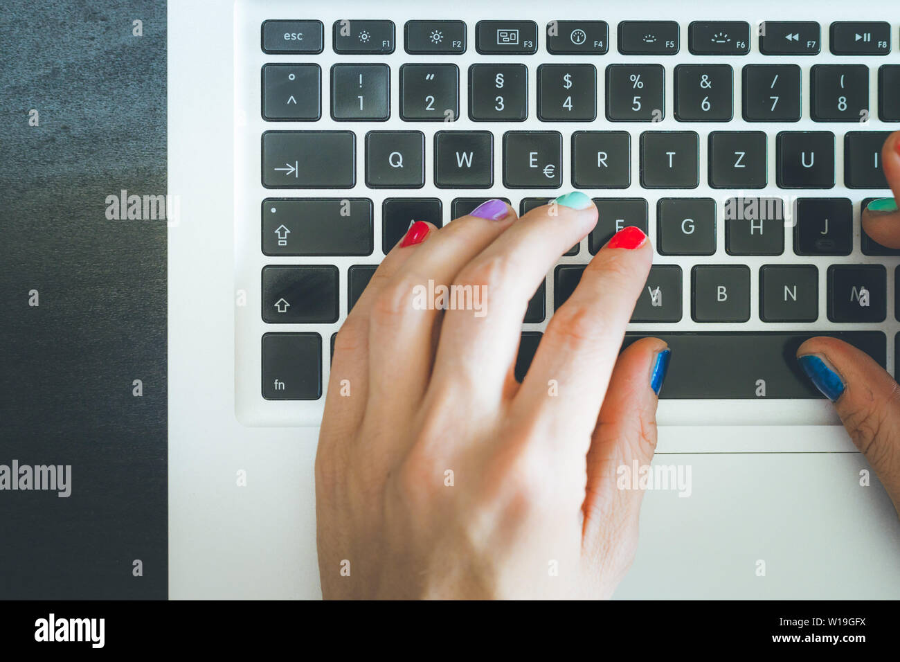 Woman fingers with colorful polished nails are typing on a laptop ...