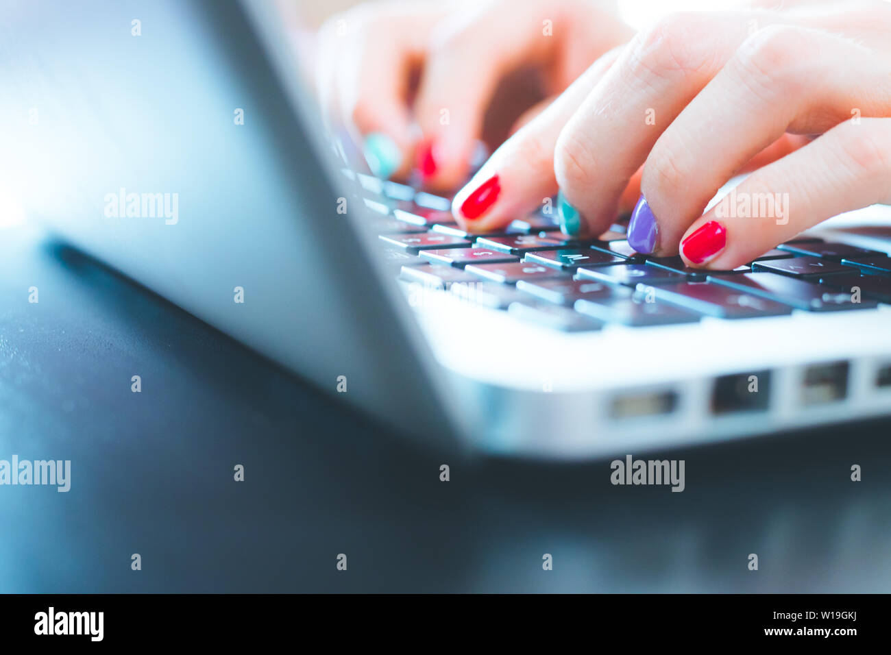 Woman fingers with colorful polished nails are typing on a laptop ...