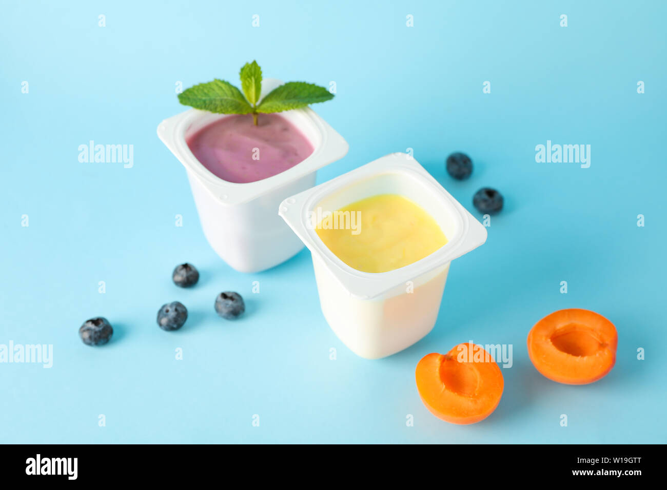 Plastic cups with yogurt and fruits on color background, space for text ...