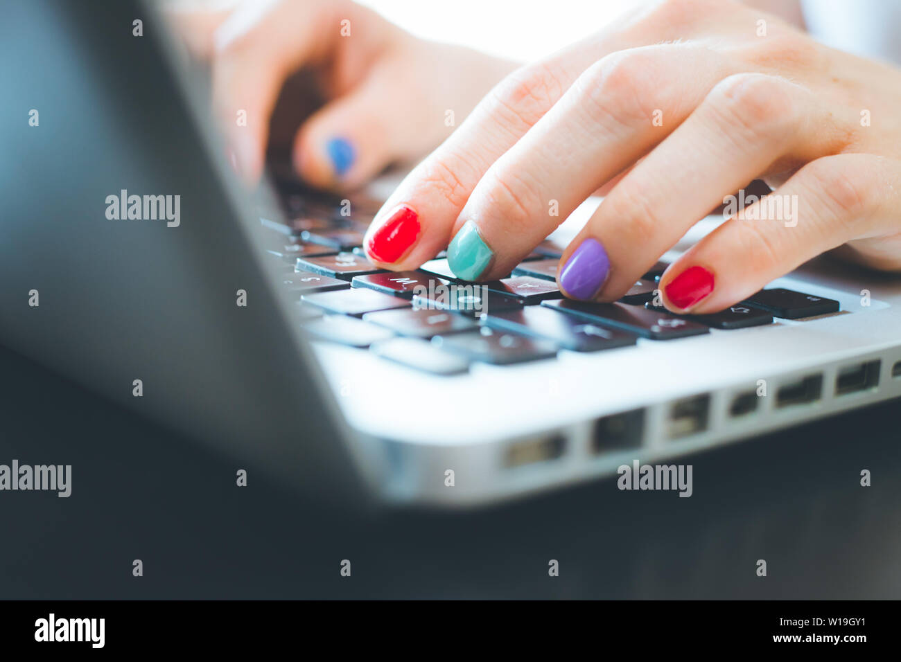 Woman fingers with colorful polished nails are typing on a laptop ...