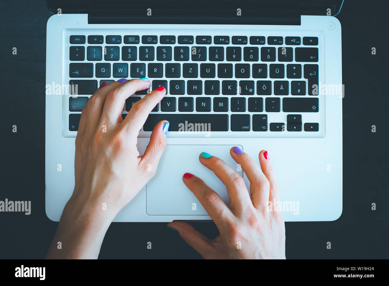 Woman fingers with colorful polished nails are typing on a laptop ...
