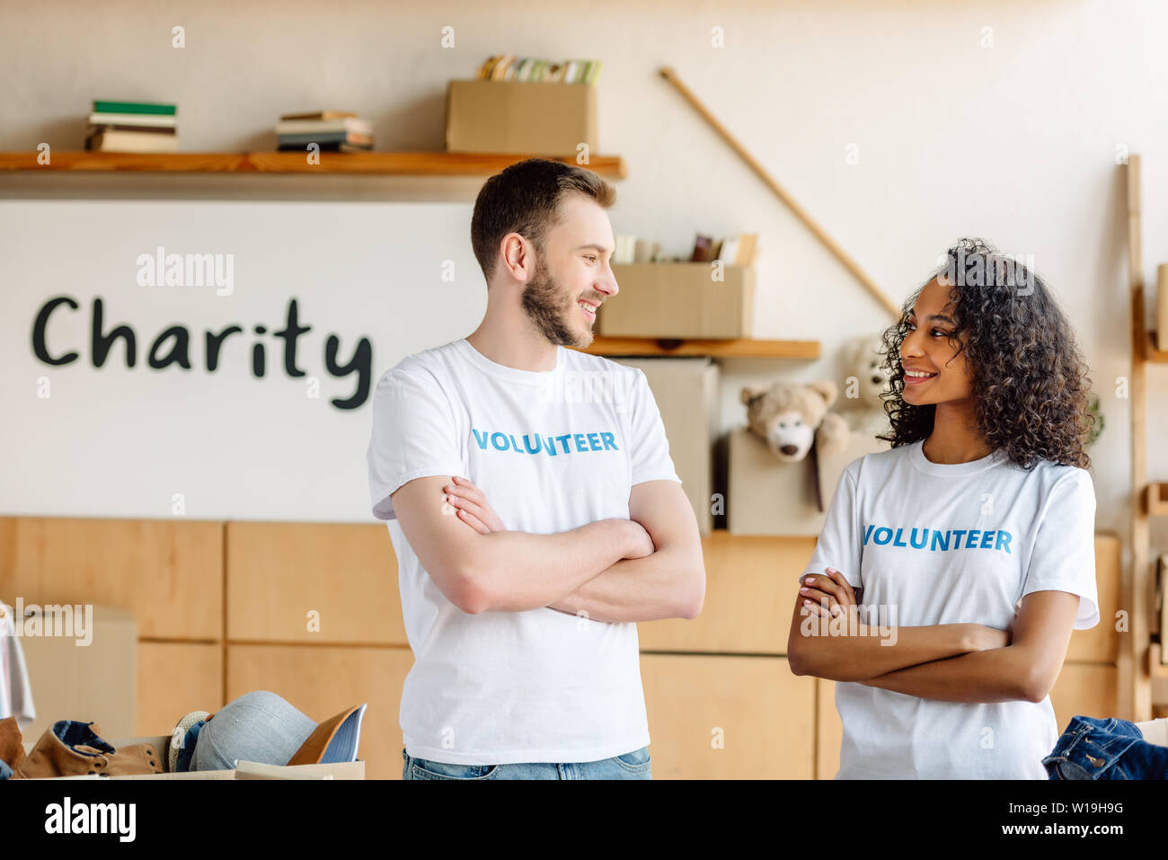 two cheerful multicultural volunteers standing with crossed arms ...