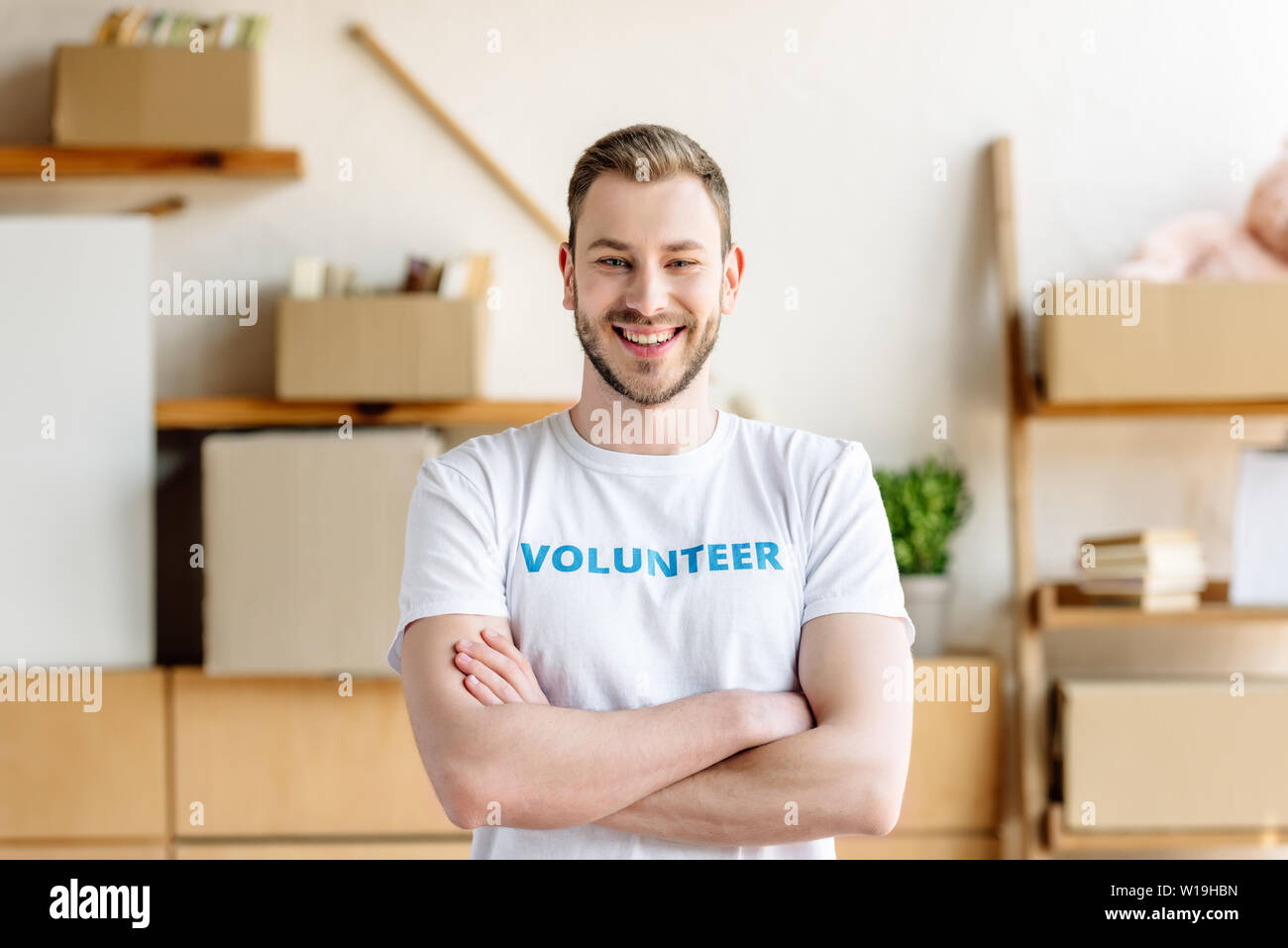 handsome young volunteer with crossed arms smiling and looking at ...
