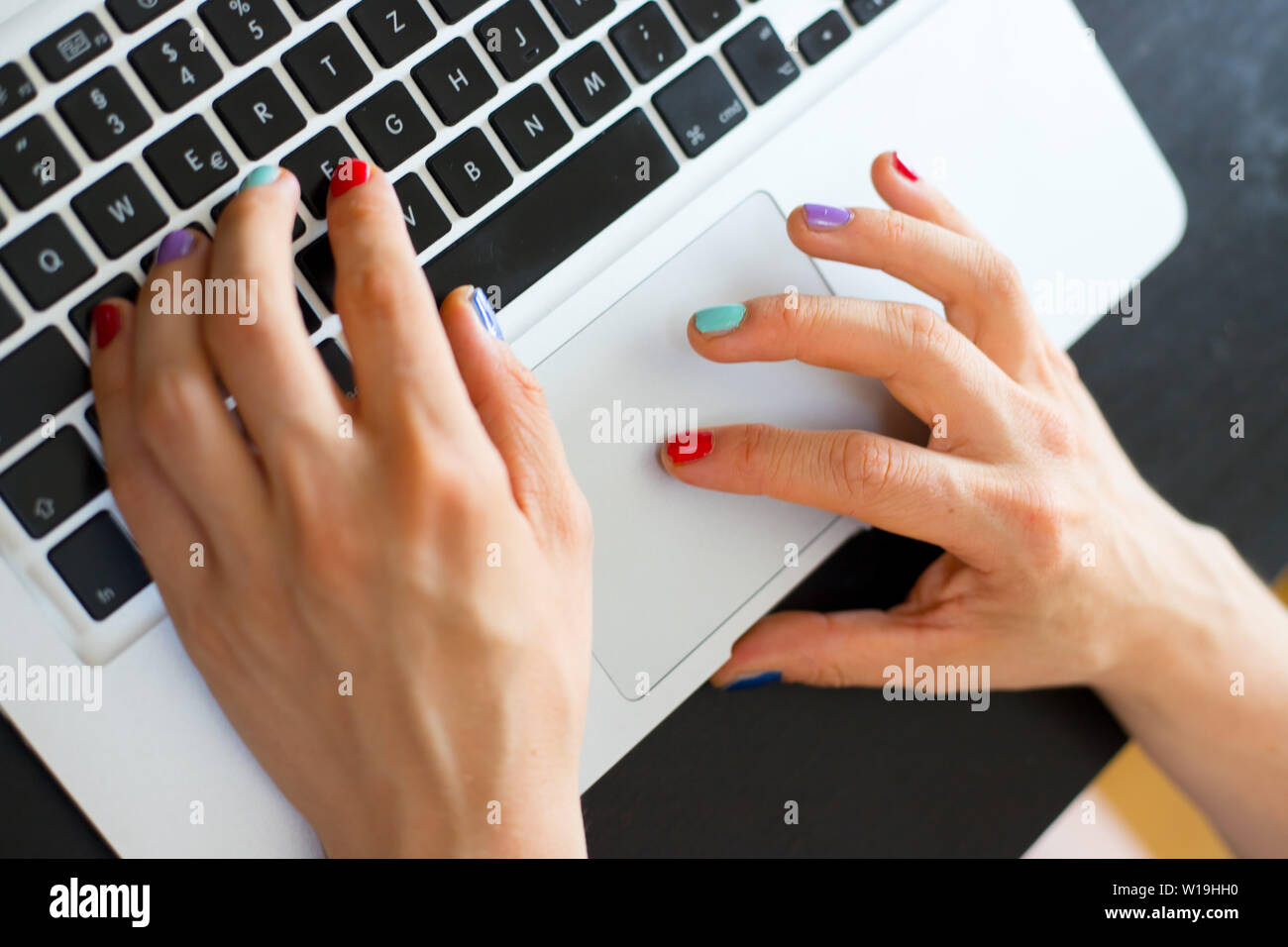 Woman fingers with colorful polished nails are typing on a laptop ...