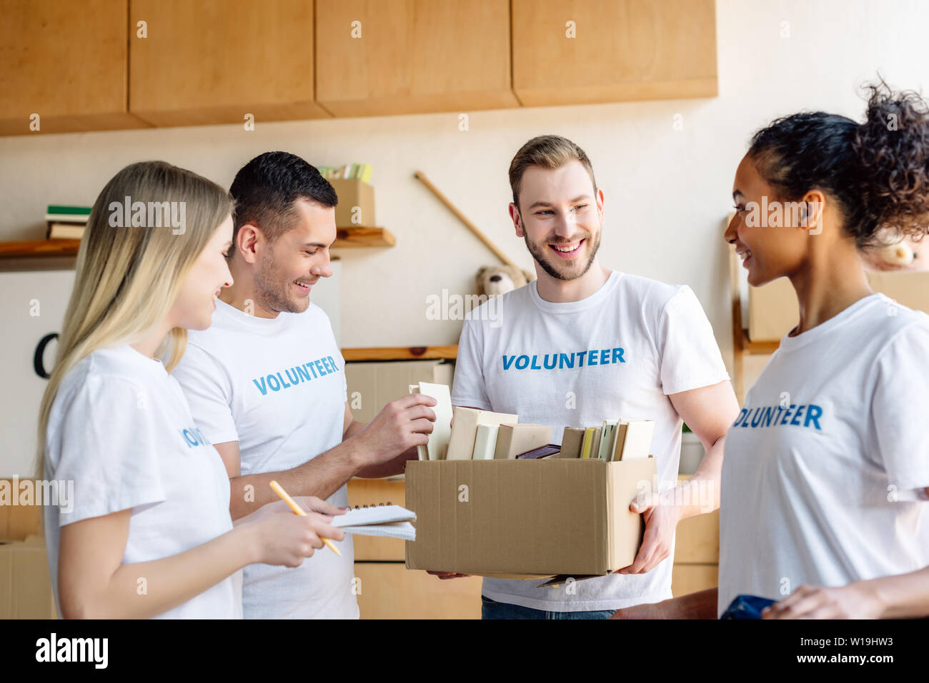 four young multicultural volunteers talking while holding cardboard box ...