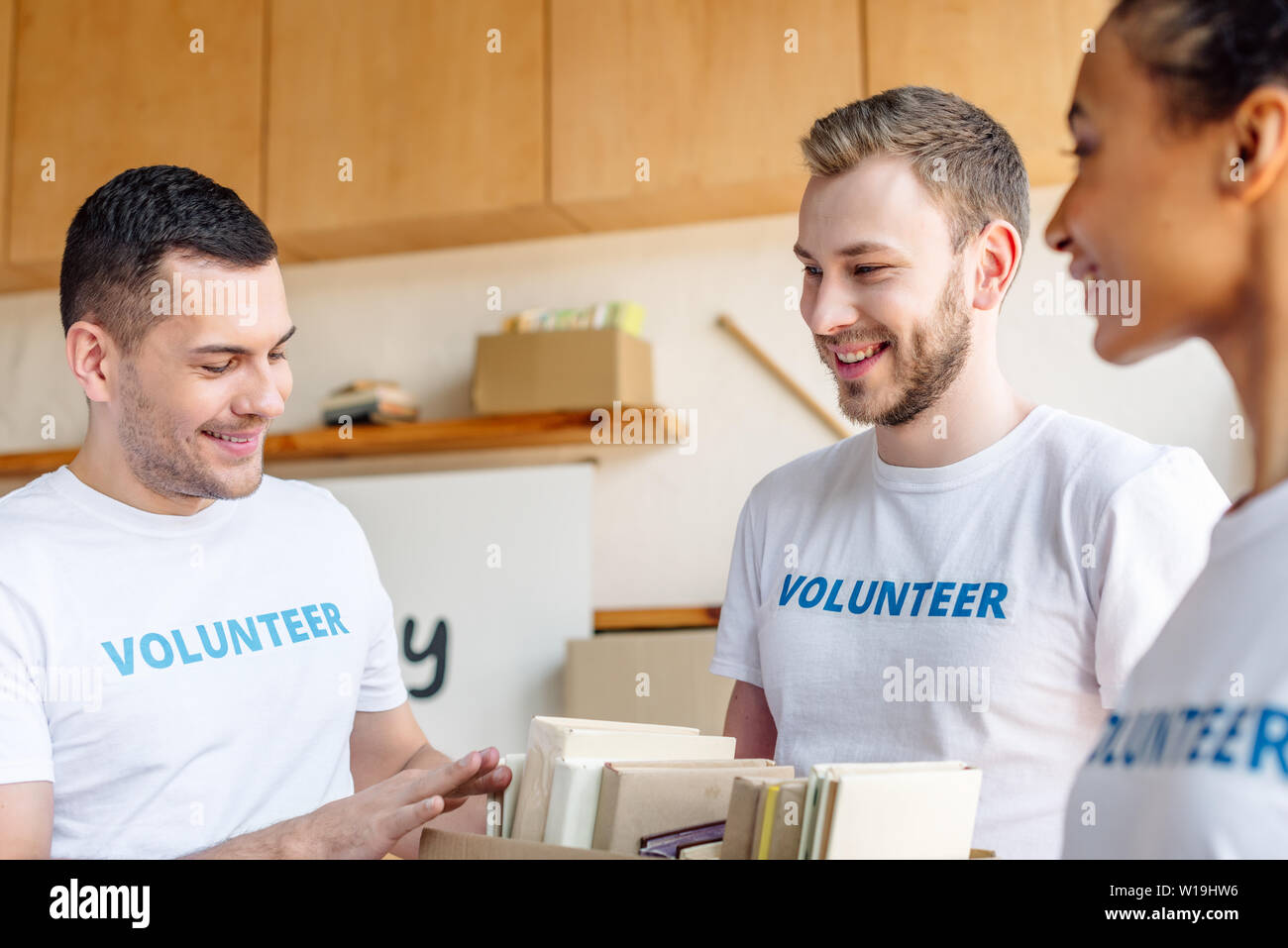 three young multicultural volunteers smiling and talking while holding ...