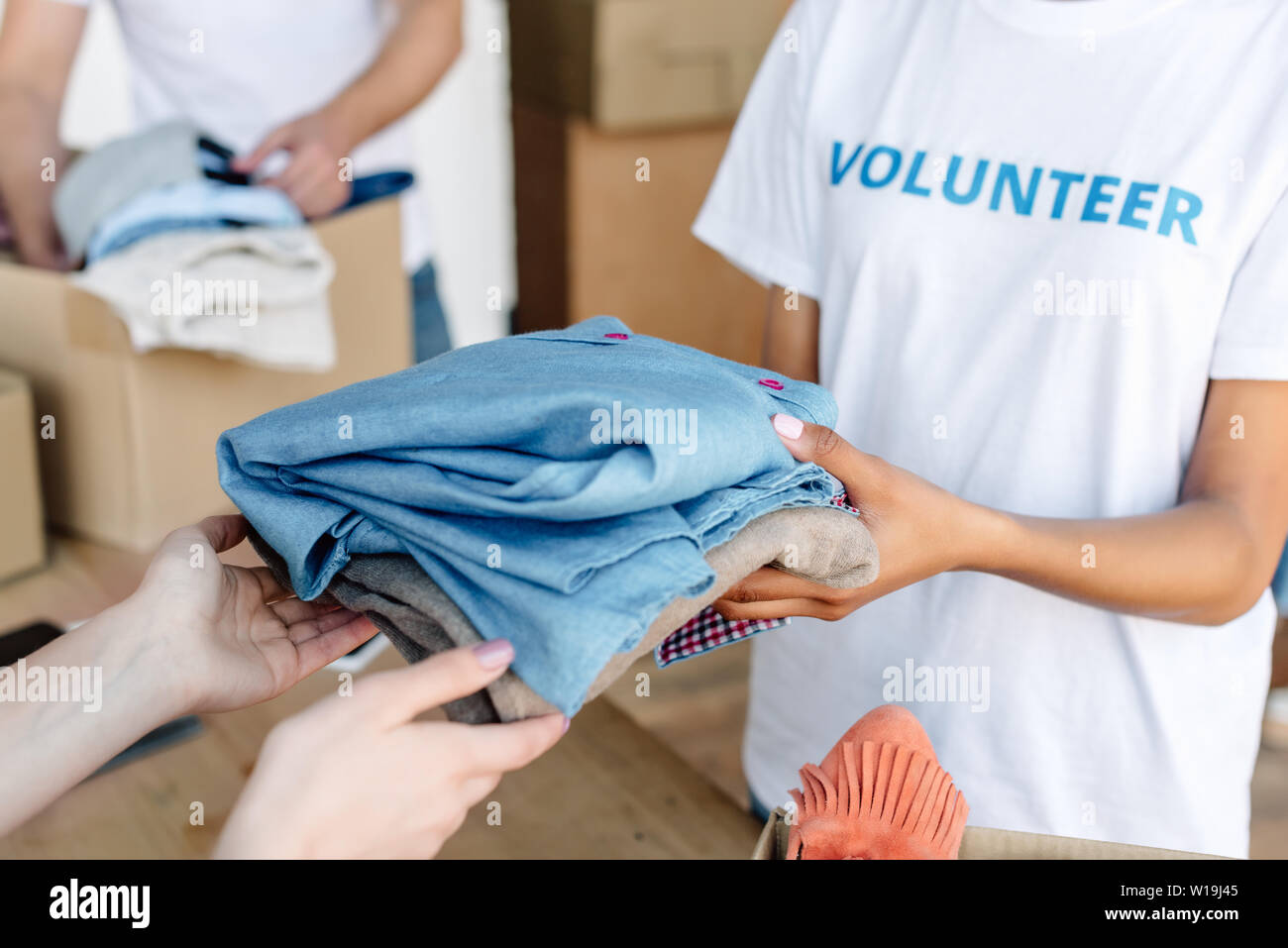 cropped view of volunteer giving clothes to woman in charity center ...
