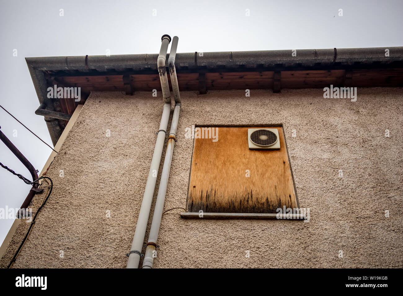 Chipboard wood covered window with old big windowed electrical fan on ...