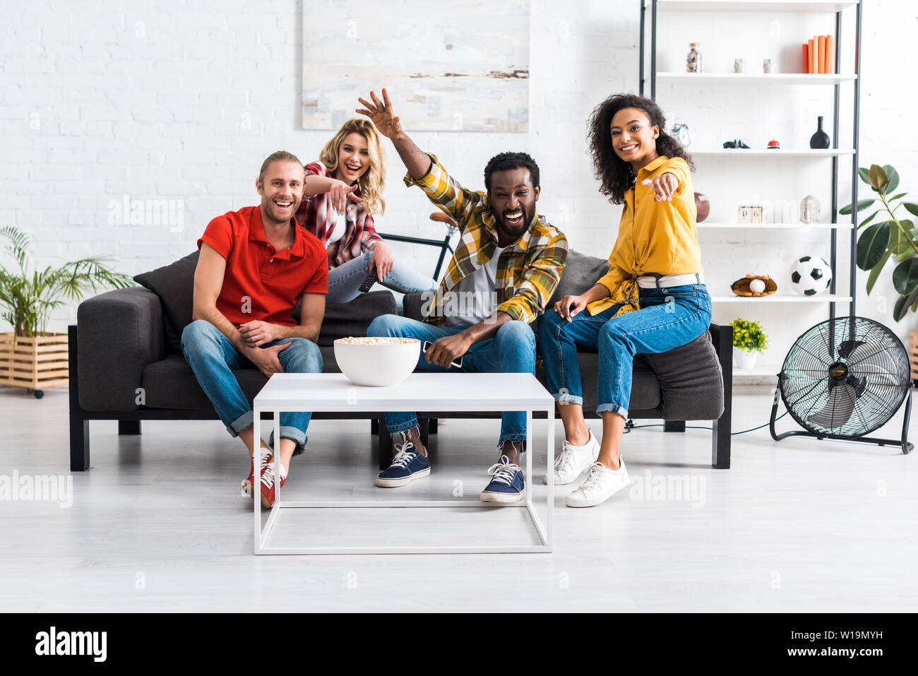 Happy laughing multicultural young people sitting on couch and spending ...