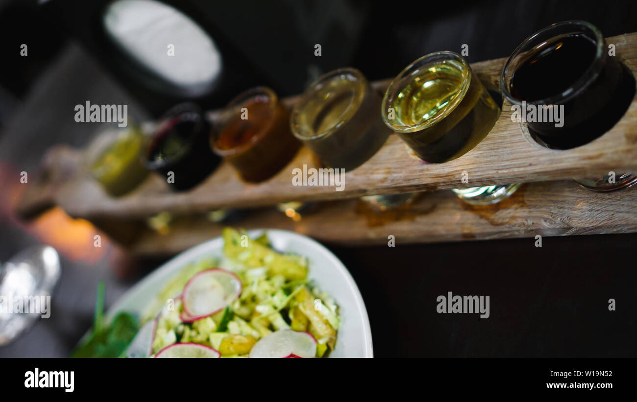 Set of shots in one row, six servings on a wooden stand and grren salad ...