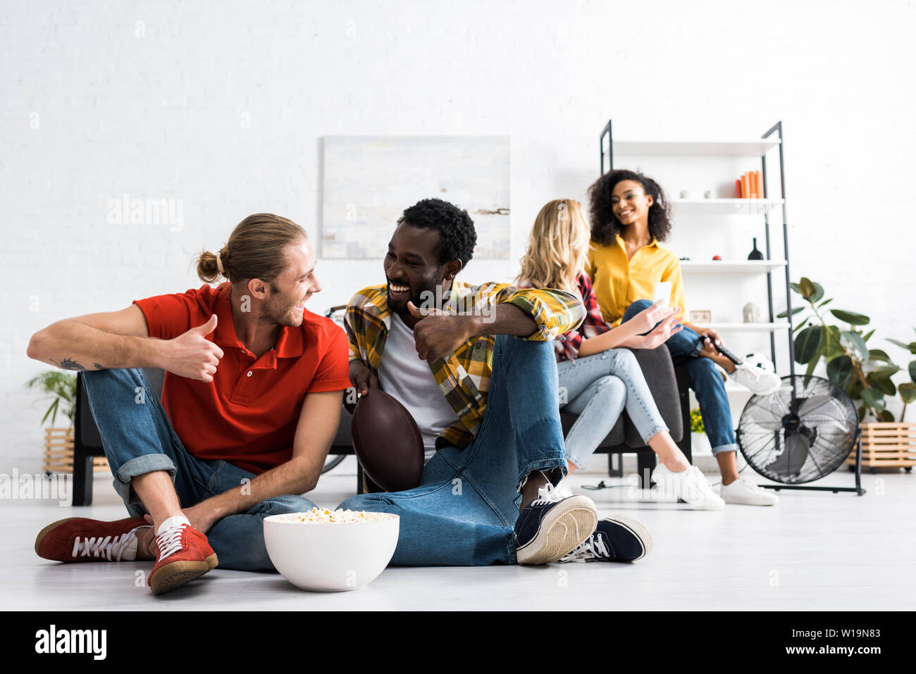 Selective focus of two smiling multicultural men sitting on floor and ...