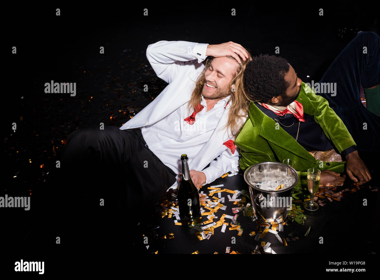 happy and drunk multicultural men lying near shiny confetti of black ...
