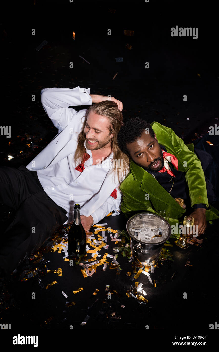 happy man smiling with closed eyes and sitting near drunk african ...