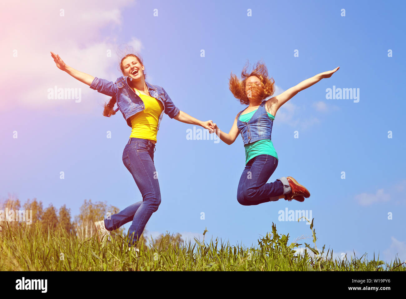 two pretty young women jumping on the sky background. happy girls ...