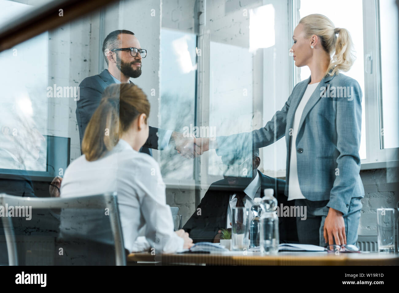 handsome bearded business coach shaking hands with blonde woman near ...